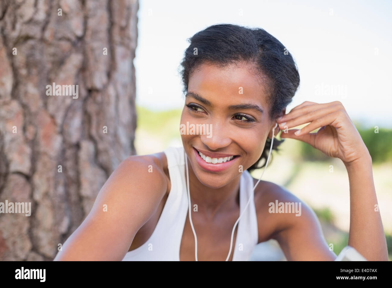 Fit woman sitting against tree listening to music Stock Photo - Alamy