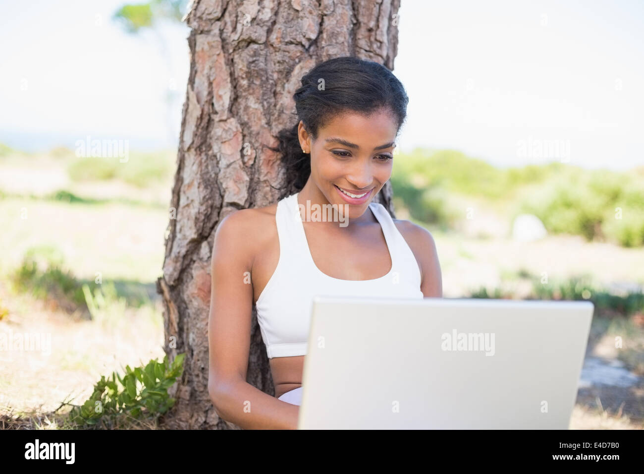 Fit woman sitting against tree using laptop Stock Photo - Alamy
