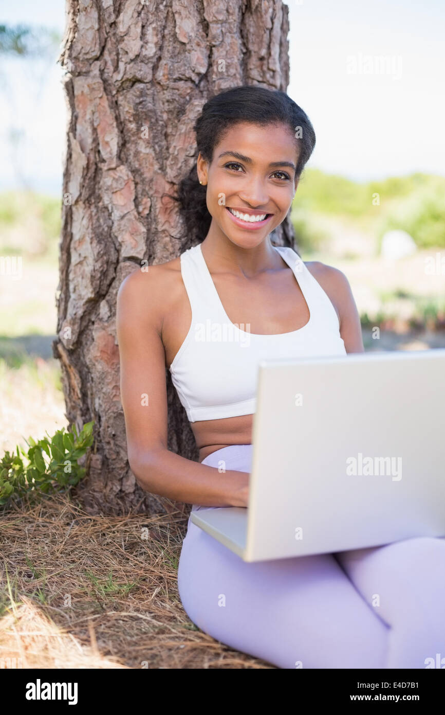 Fit woman sitting against tree using laptop Stock Photo - Alamy