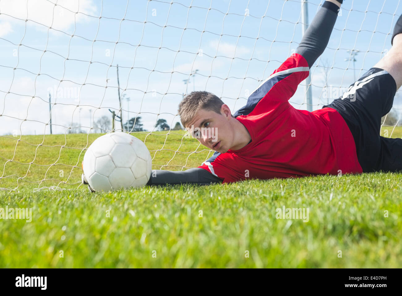 Goalkeeper in red making a save in a large football stadium with lights ...