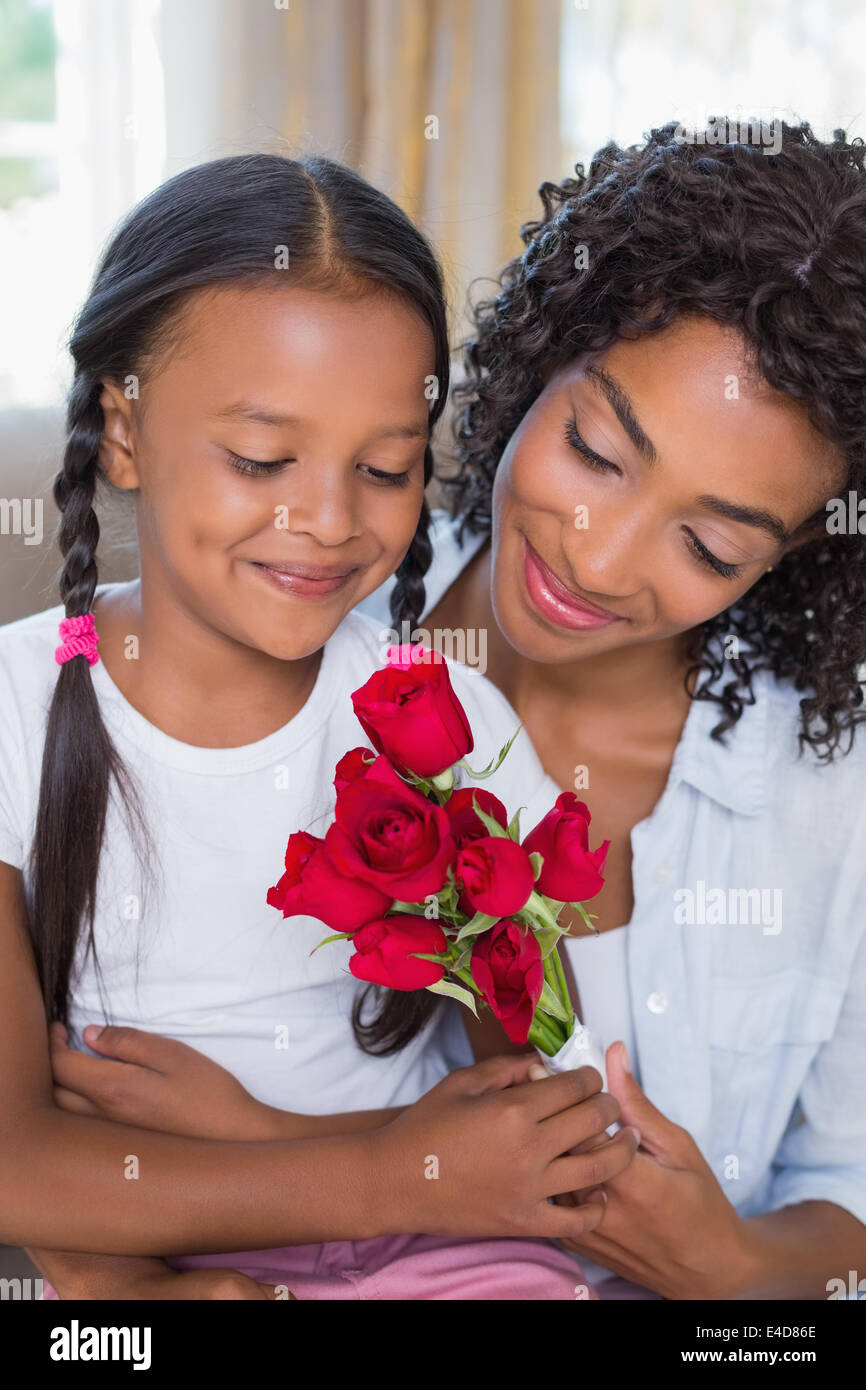 Pretty mother sitting on the couch with her daughter holding roses ...