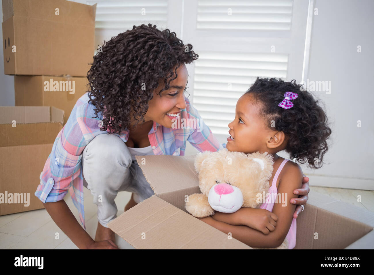 Cute daughter sitting in moving box holding teddy with mother Stock ...