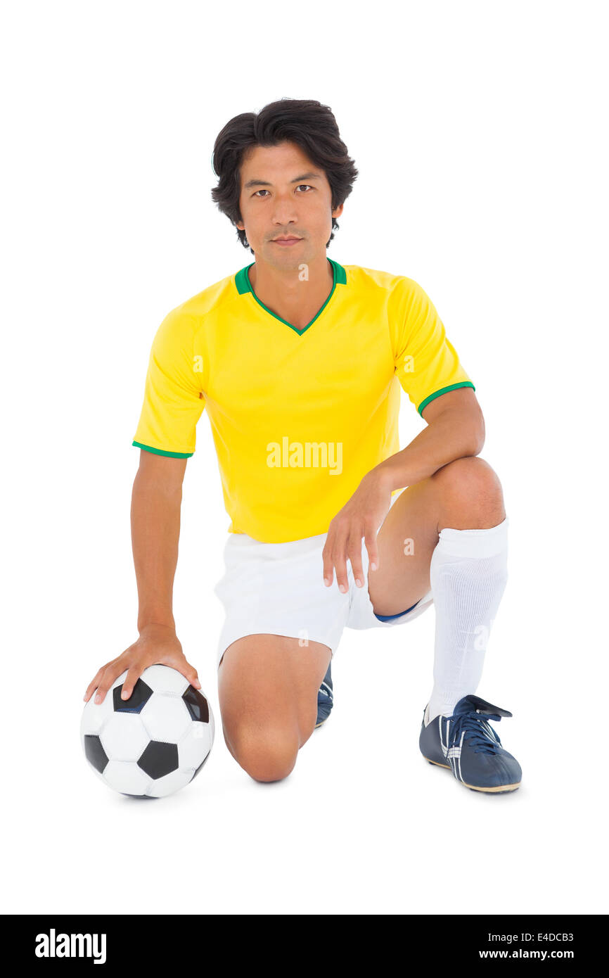 Football player in yellow kneeling with ball Stock Photo - Alamy
