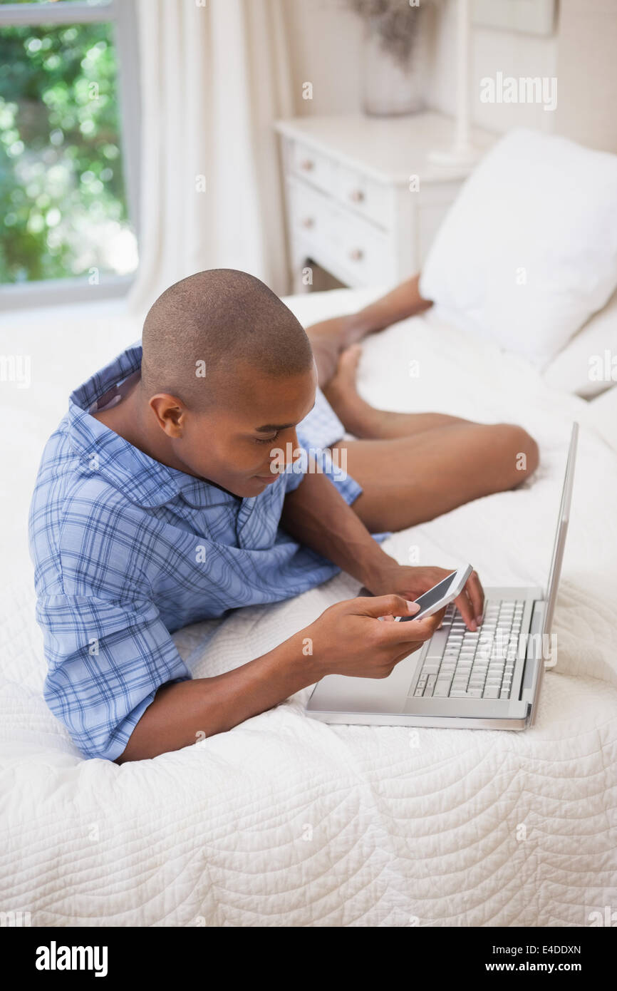 Happy man using laptop on bed while texting Stock Photo - Alamy