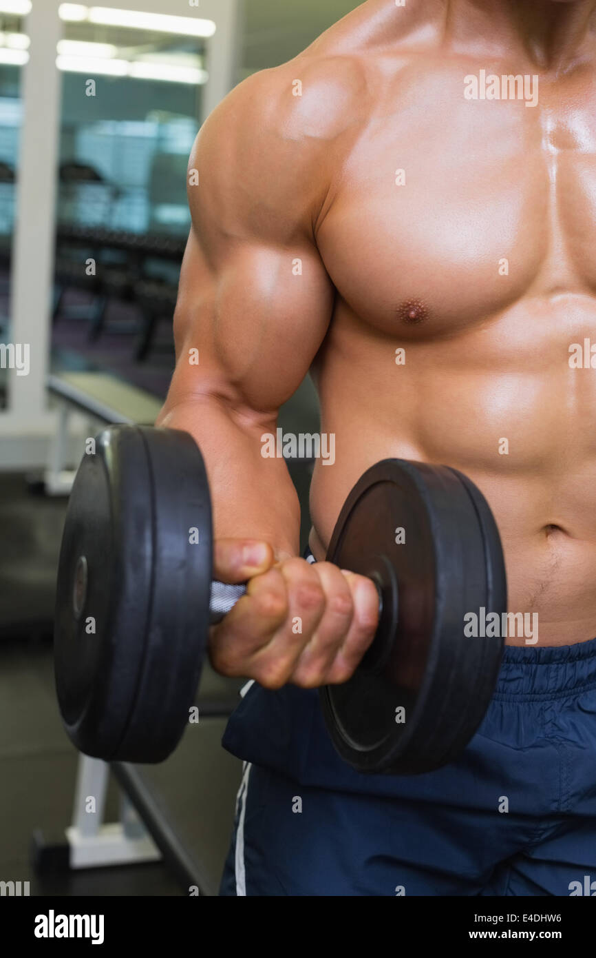 Mid section of shirtless young muscular man exercising with dumbbell ...
