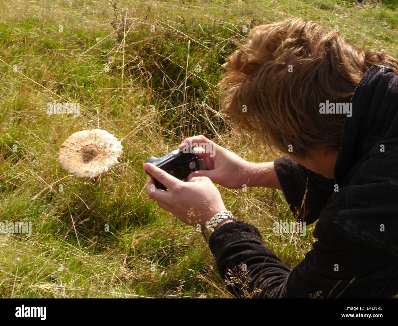 A man taking a close-up picture of a toadstool with a compact camera ...
