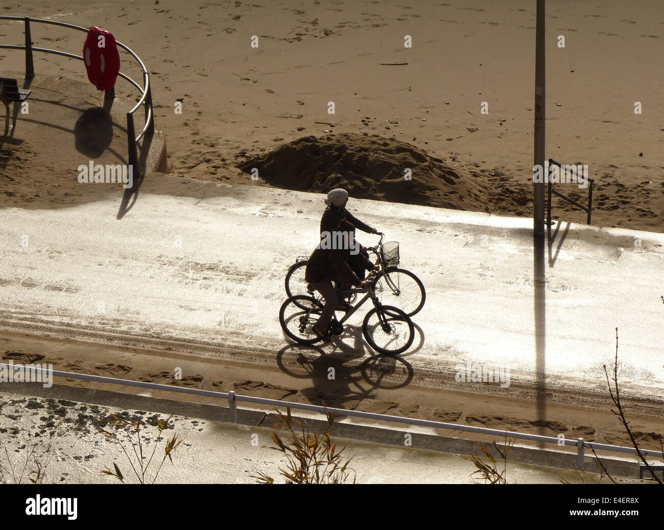 An overhead shot of two people cycling along a beach front esplanade ...