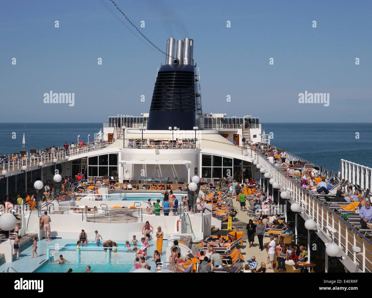 The top deck of a busy cruise ship with people sitting around the pool ...
