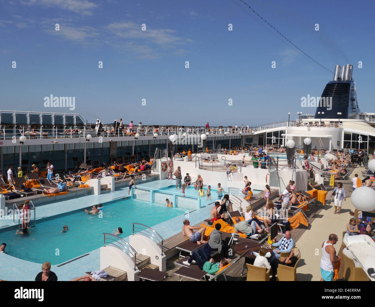 The top deck of a busy cruise ship with people sitting around the pool ...