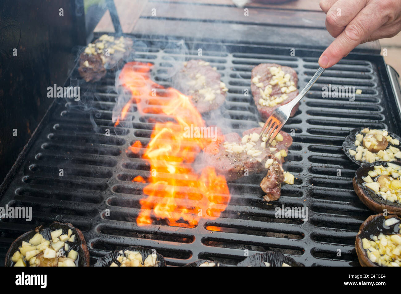 Man barbecuing steak and mushrooms with garlic using a gas fired ...