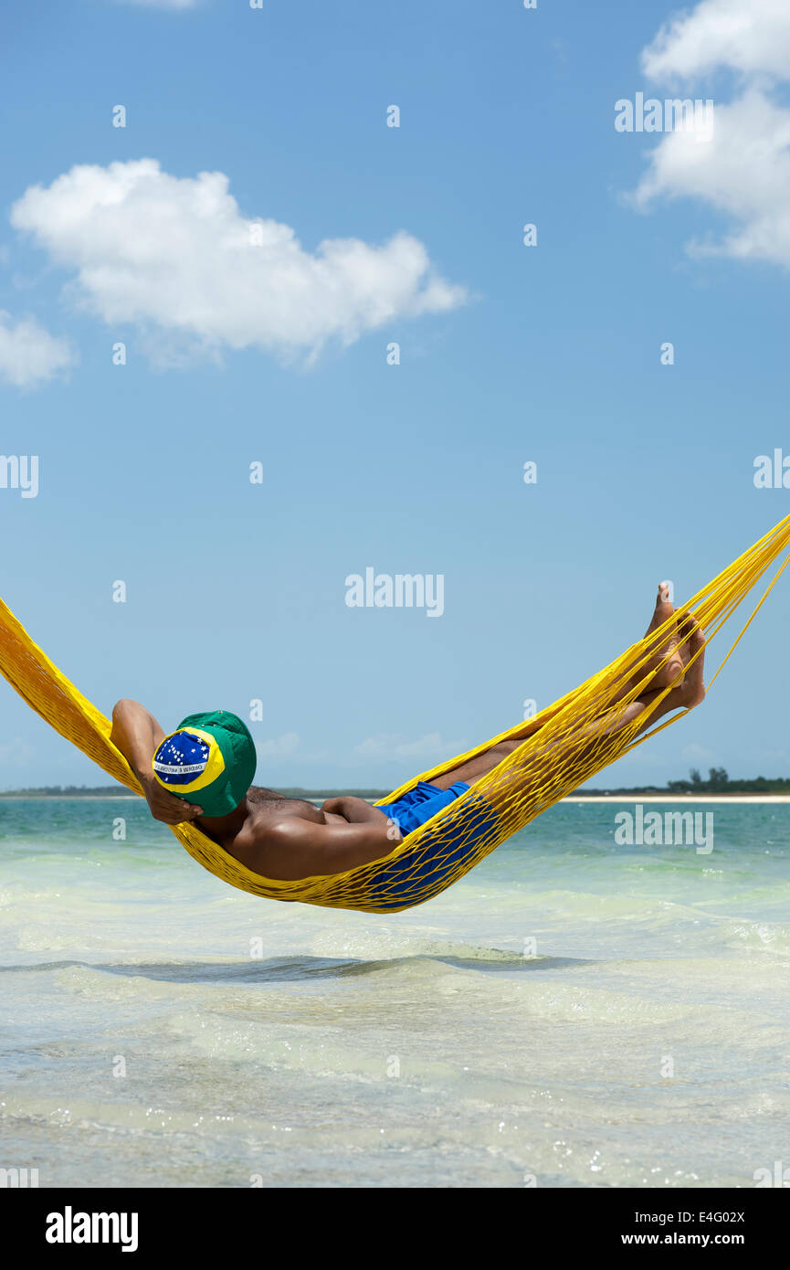 Brazilian man relaxing in beach hammock over shallow sea waters Stock ...