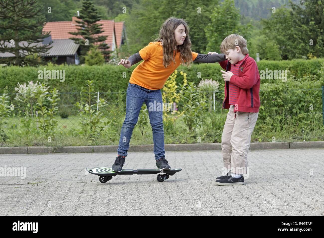 young boy supporting young girl on a caster board Stock Photo - Alamy