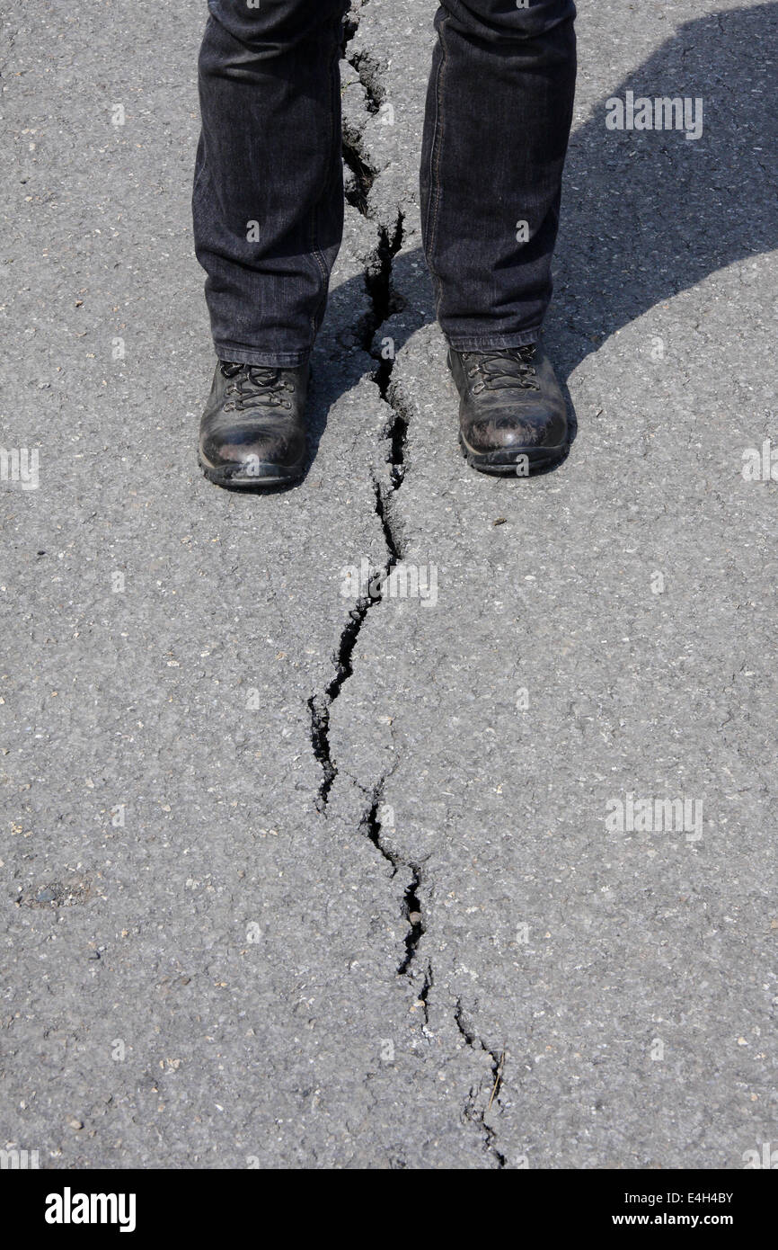 A person stands over a crack caused by a landslide on a now disused ...