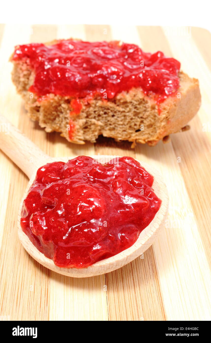 Homemade strawberry jam on wooden spoon and portion of whole wheat ...