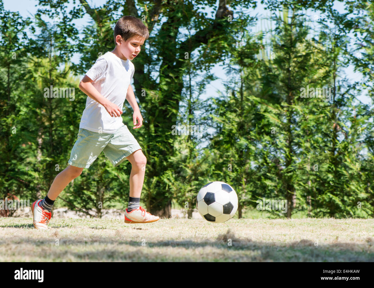 Child playing football in a stadium. Trees on the background Stock ...