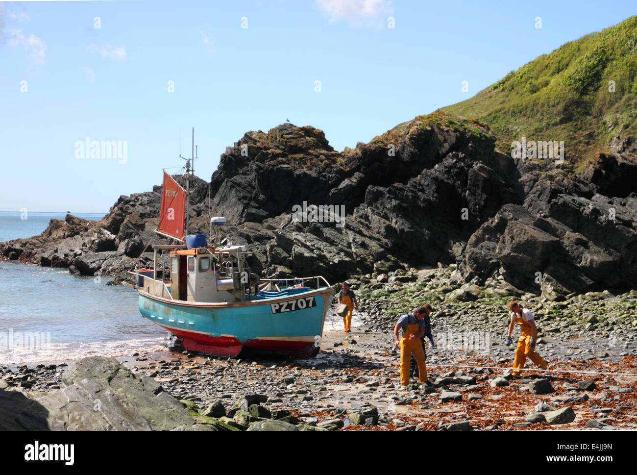 A blue fishing boat with a red mizzen sail beached on a rocky seashore ...