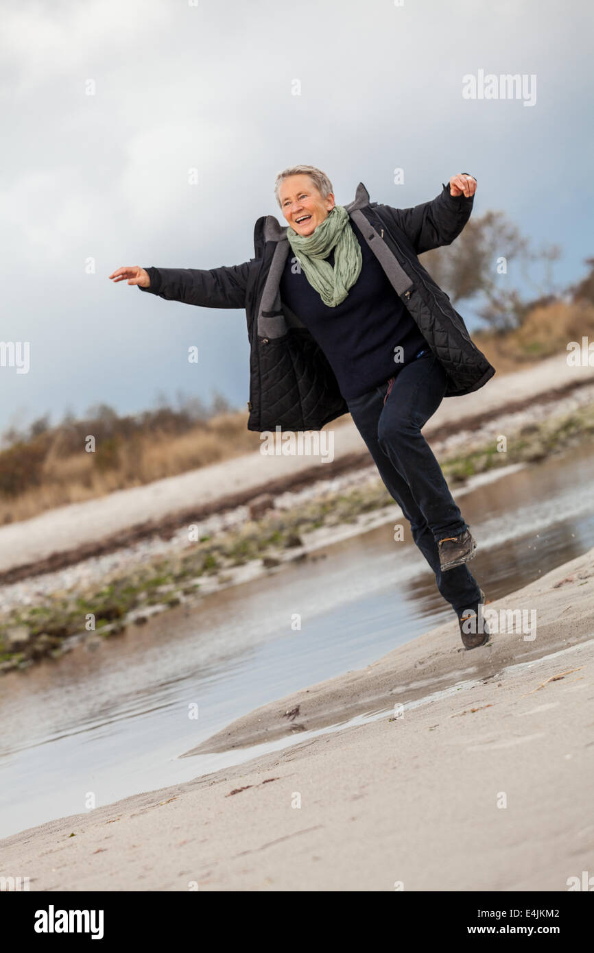Happy senior woman frolicking on the beach striding along with ...