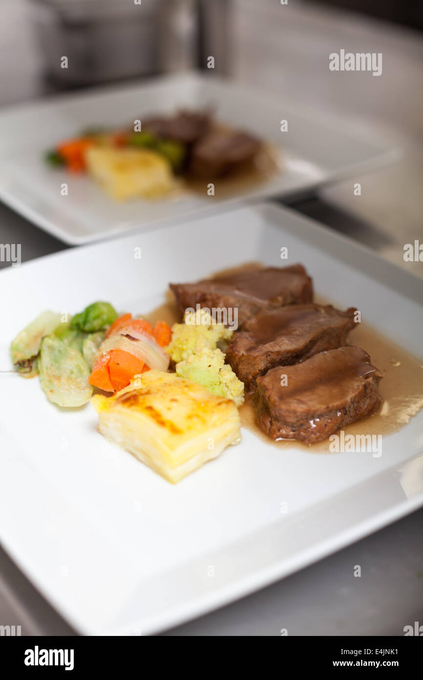 Chef plating up food in a restaurant pouring a gravy or sauce over the ...
