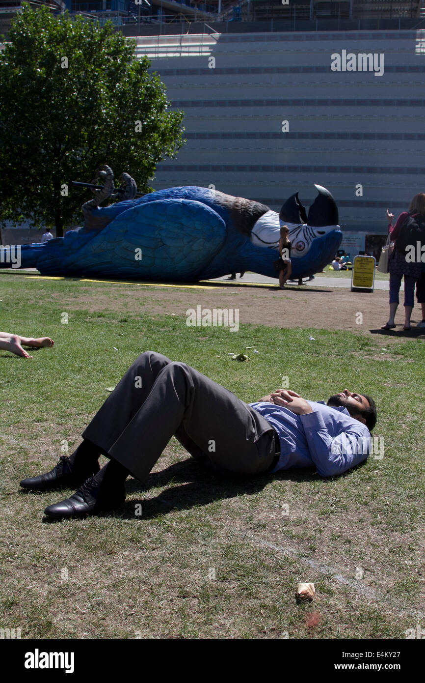 London UK. 14th July 2014. A man relaxes in front of a giant sculpture ...