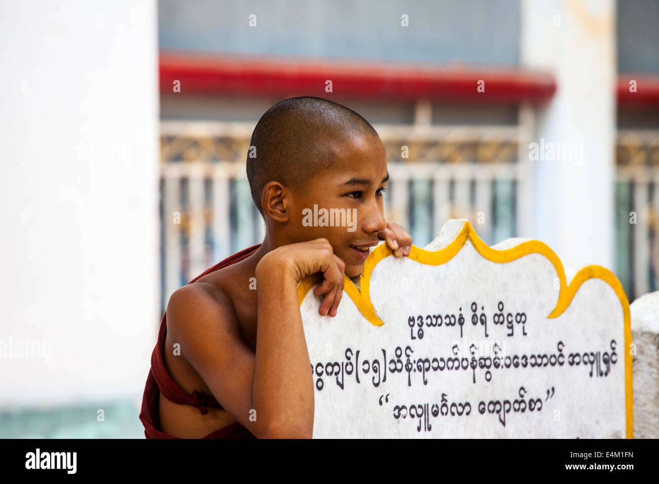 A young monk rests on a large tablet of Buddhist script while he waits ...
