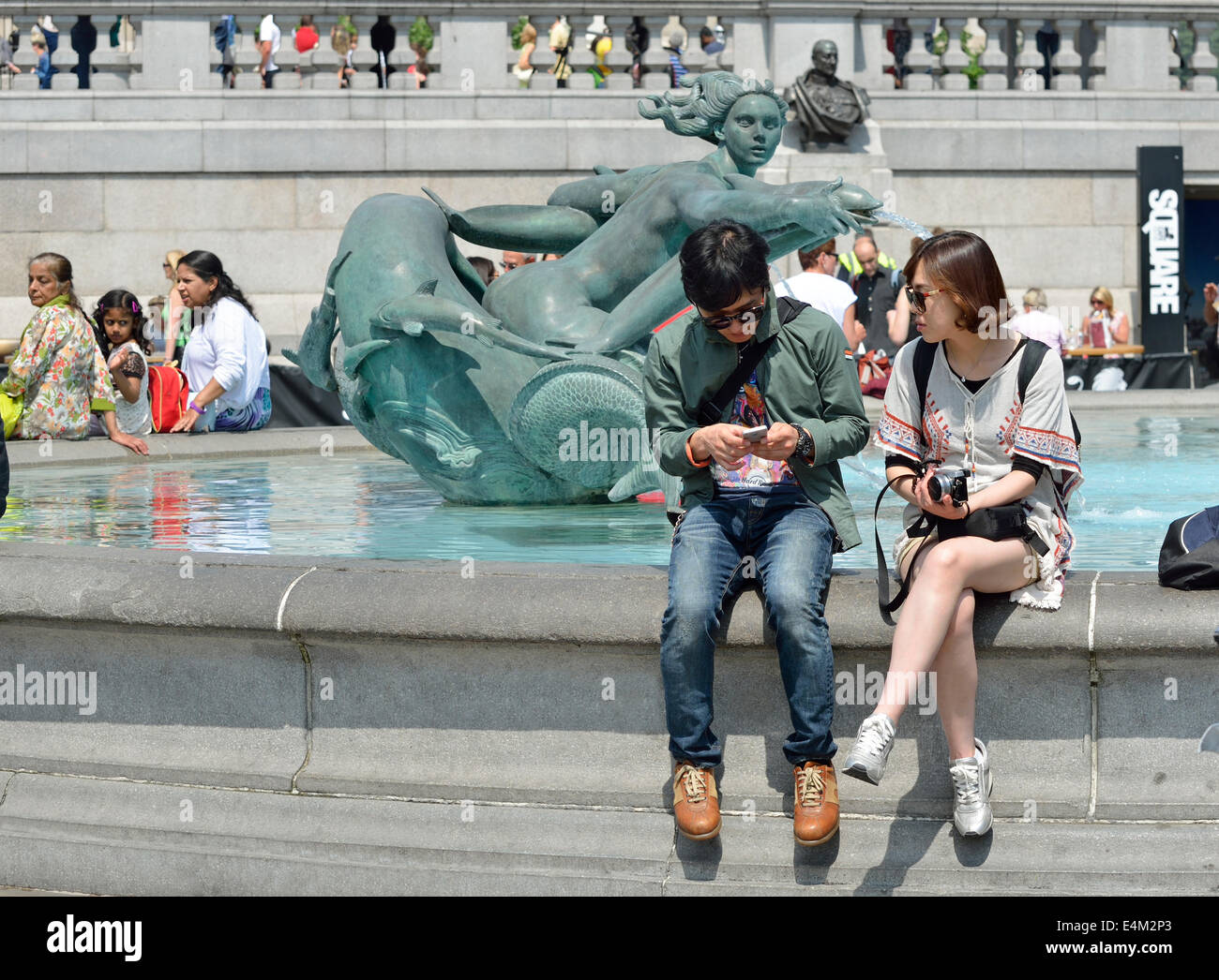 London, England, UK. Young Asian couple relaxing in Trafalgar Square ...