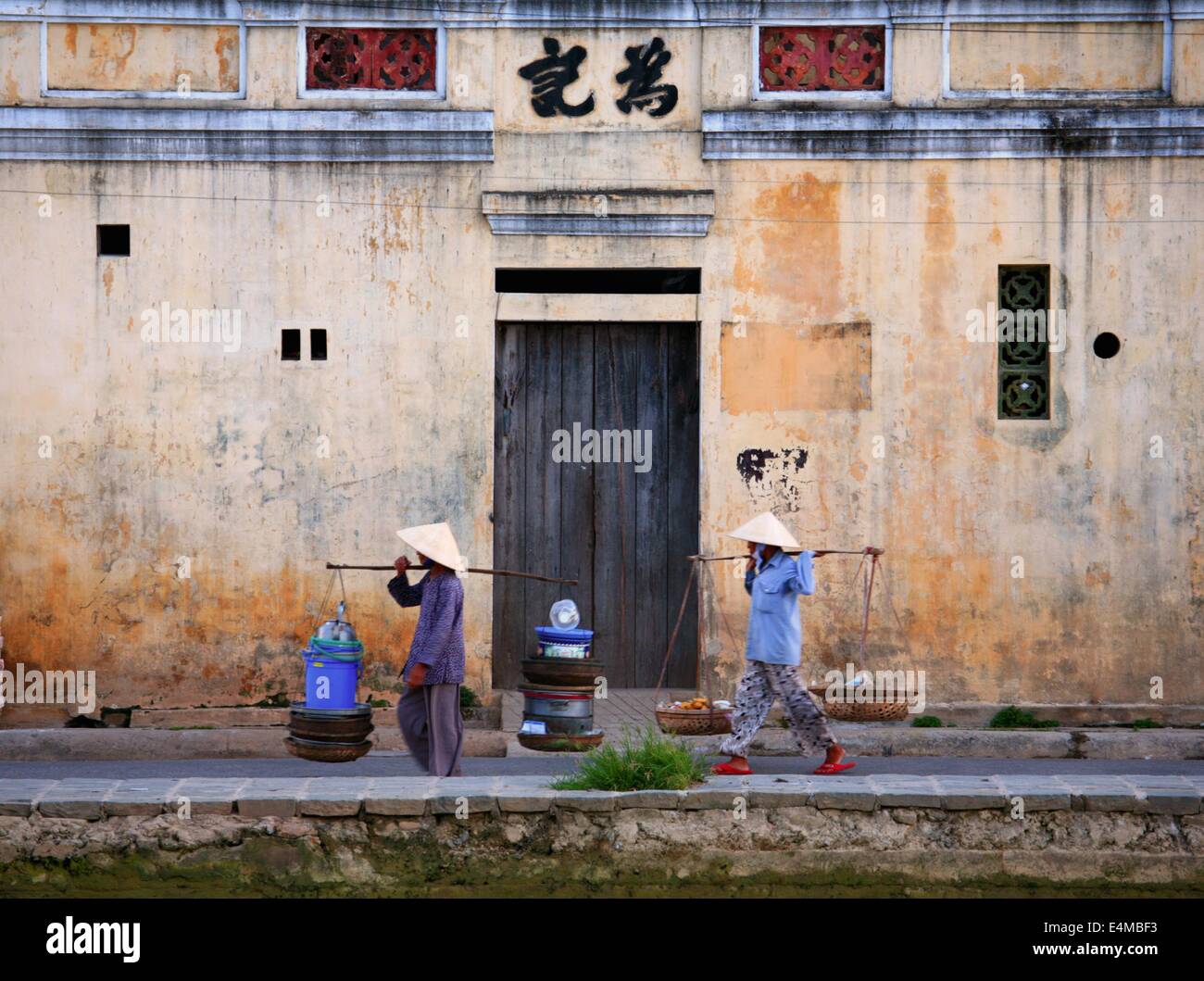 People walk carrying heavy loads using traditional methods in Hoi An ...