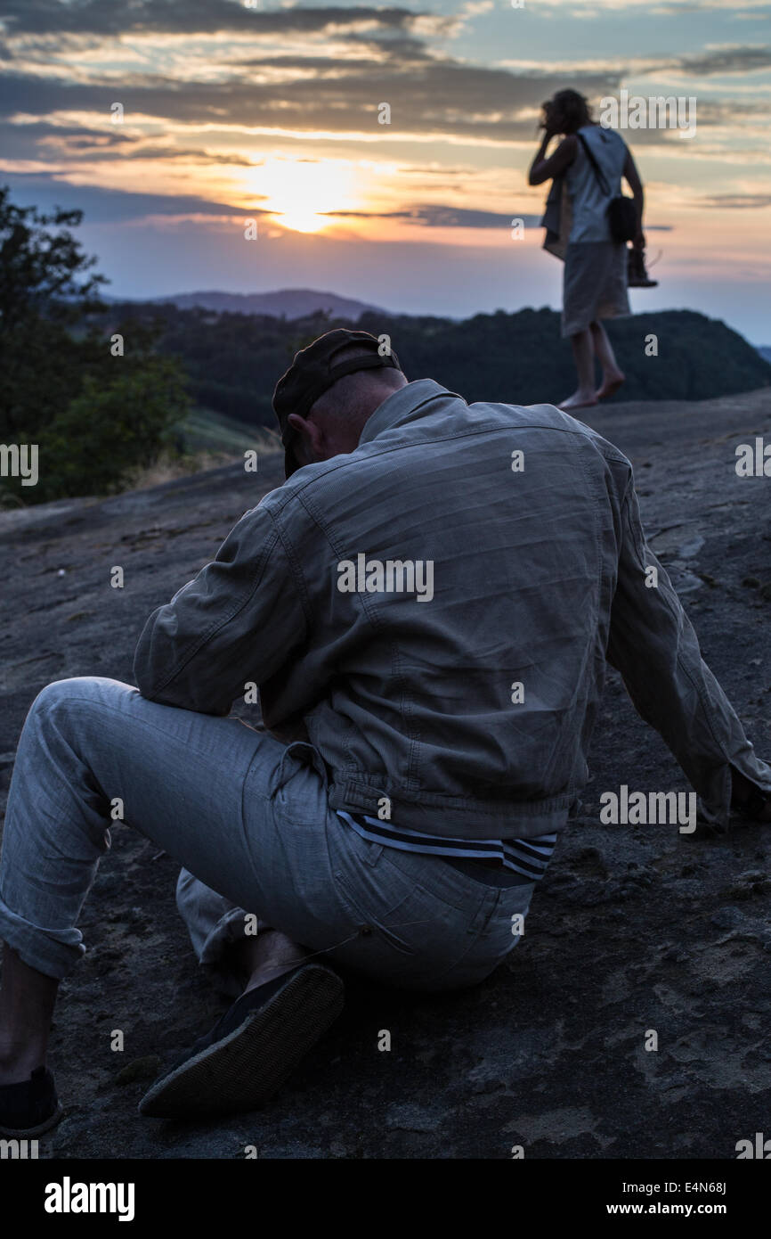man in foreground sitting on rock with back to us discussing with woman ...