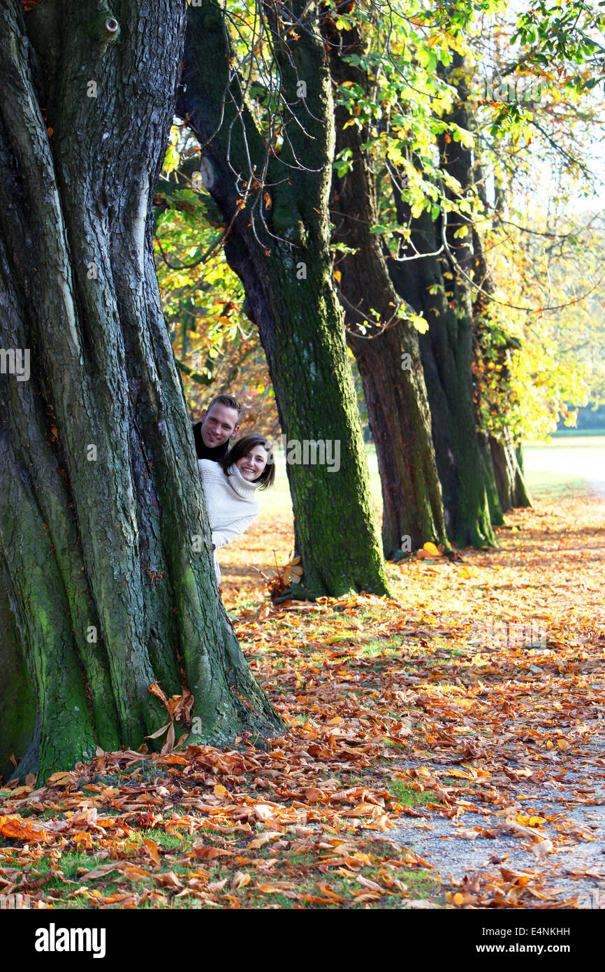 Playful couple peering around an autumn tree Stock Photo - Alamy