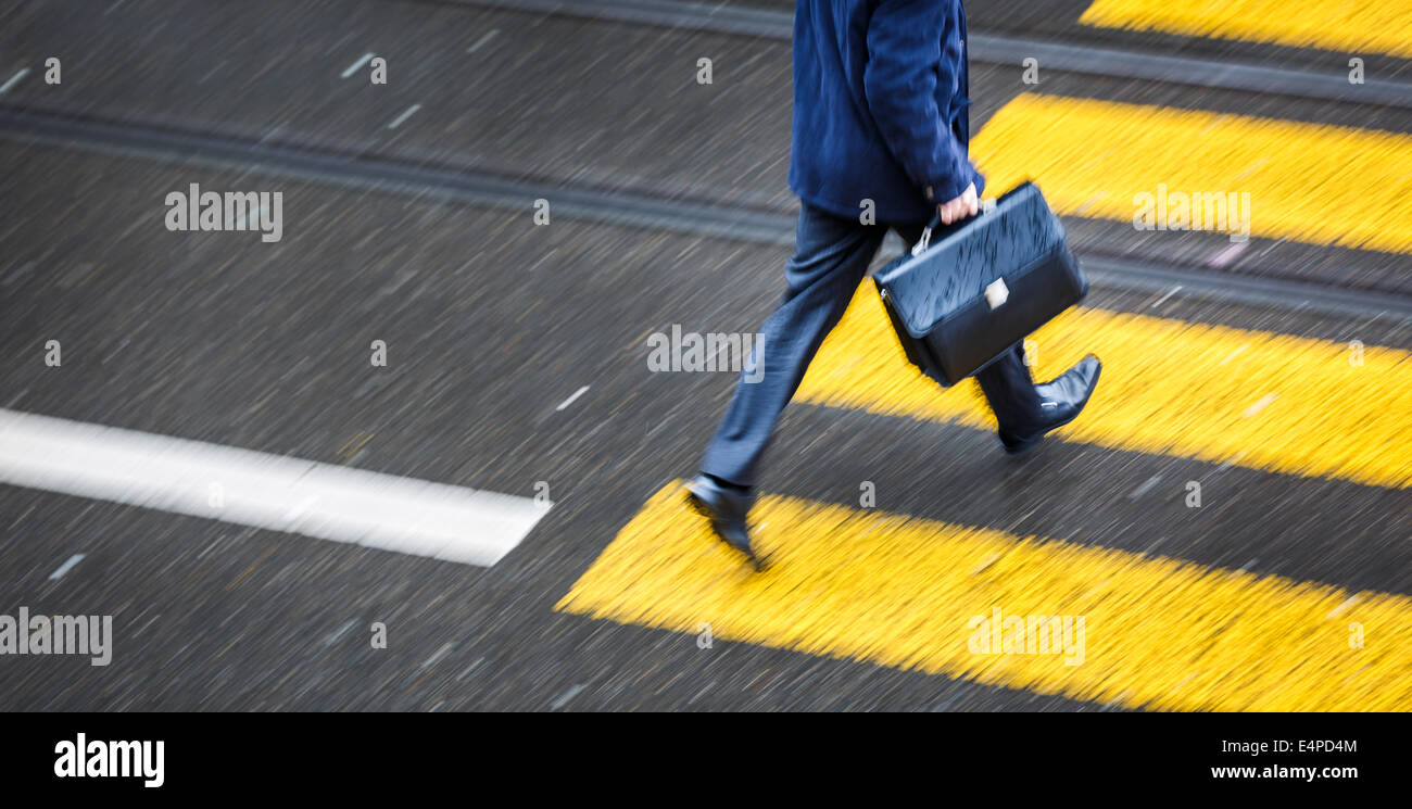 Man rushing over a road crossing in a city on a rainy day (motion ...