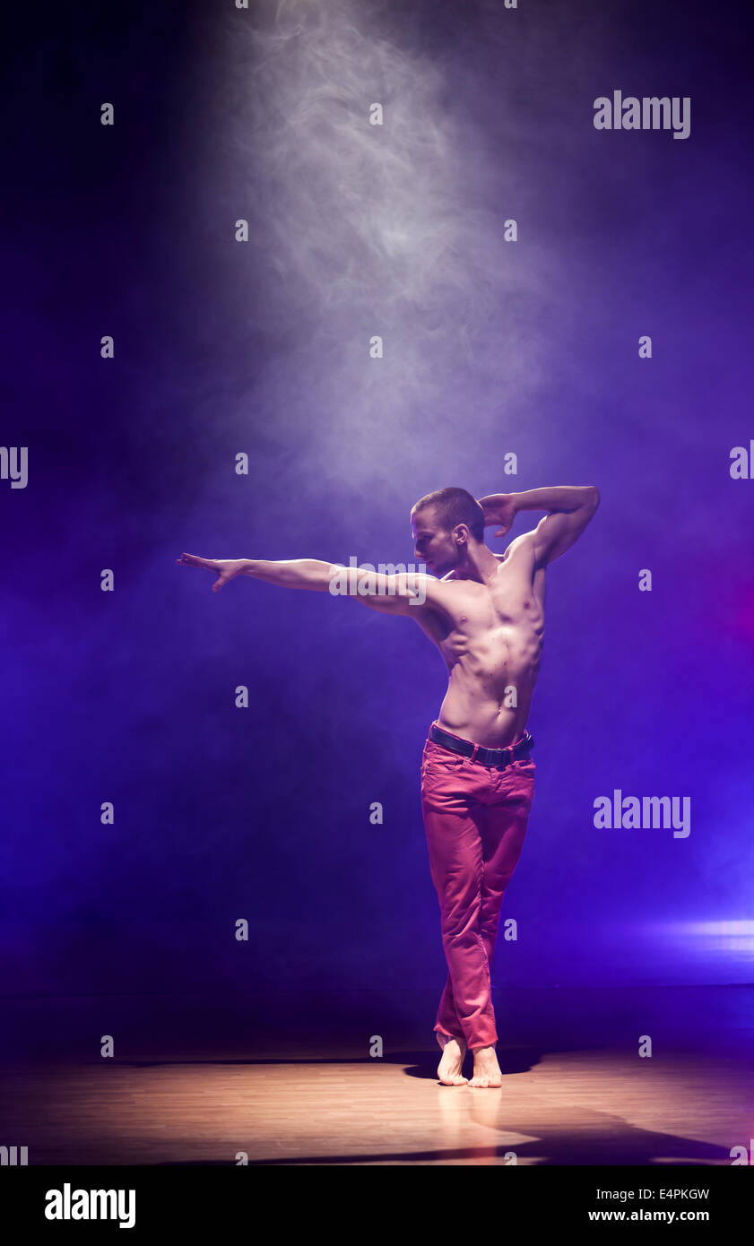 Young and muscular man performing a contemporary dance pose on a stage ...