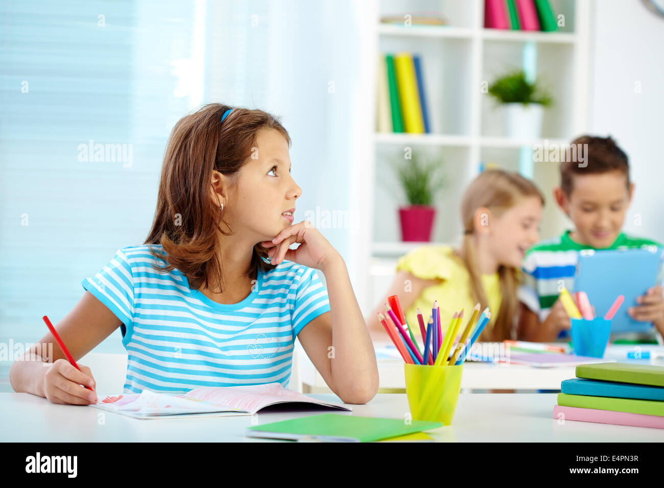Portrait of pensive girl drawing at workplace with her schoolmates on ...