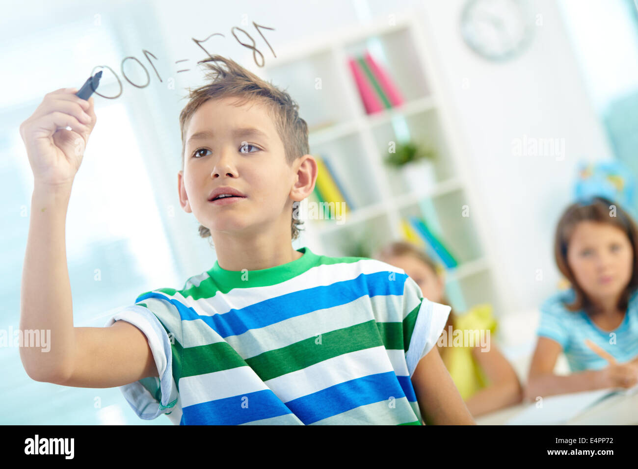 Portrait of clever boy doing sums on transparent board with schoolmates ...