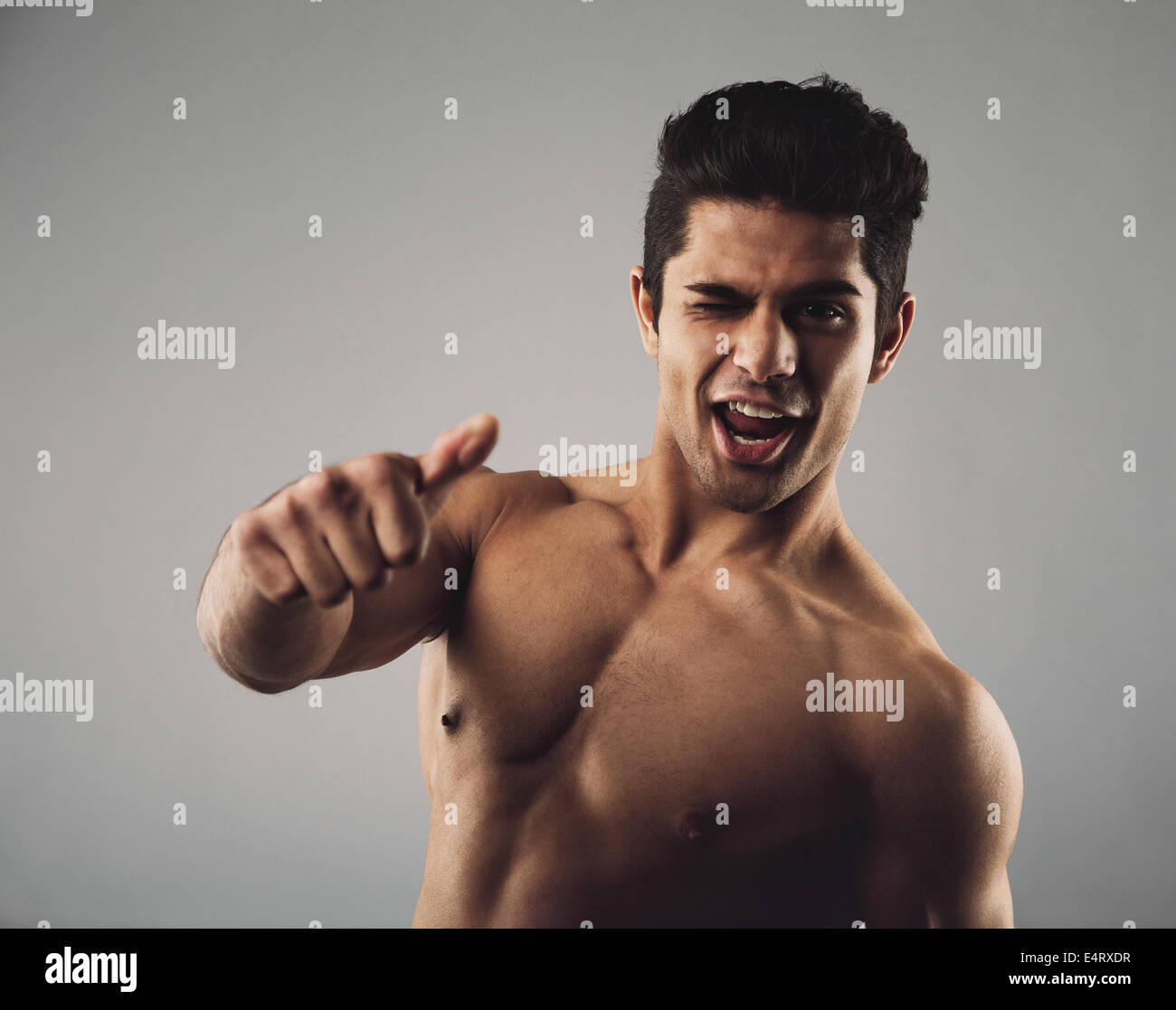 Portrait of a happy young man with muscular physique winking and giving ...