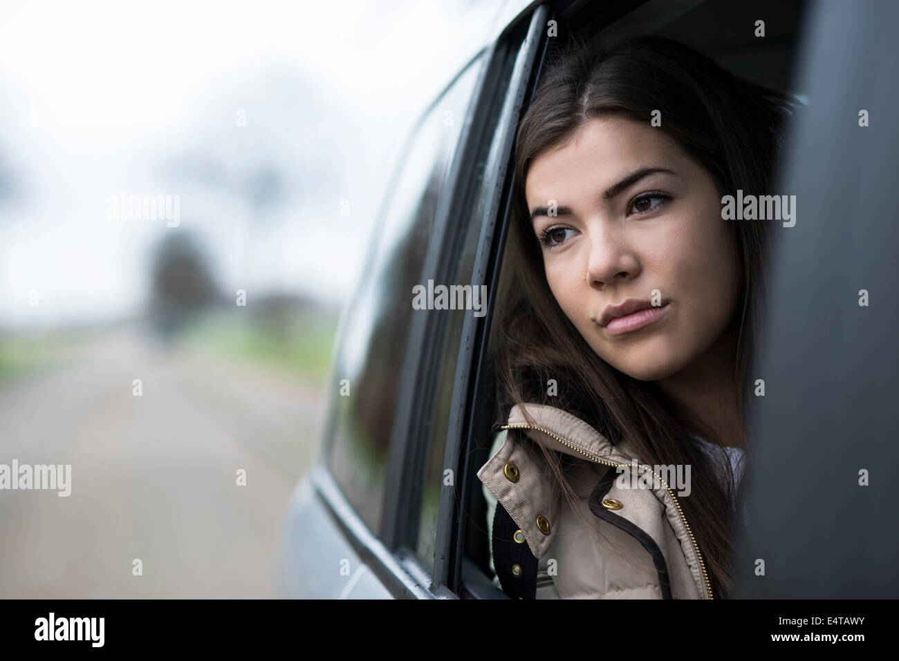 Portrait of young woman sitting inside car and looking out of window ...