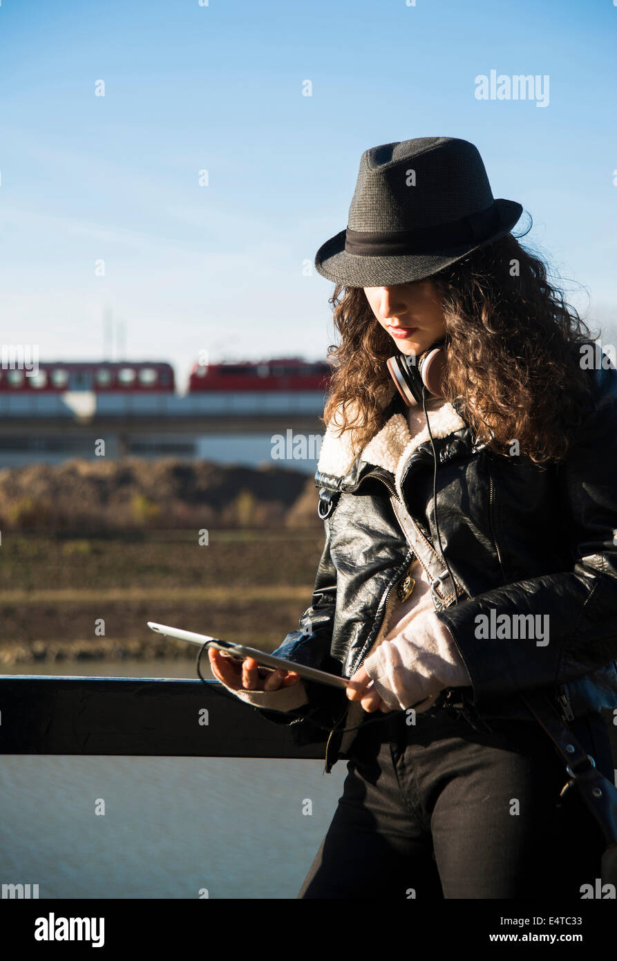 Teenage girl standing outdoors, wearing fedora and using tablet ...