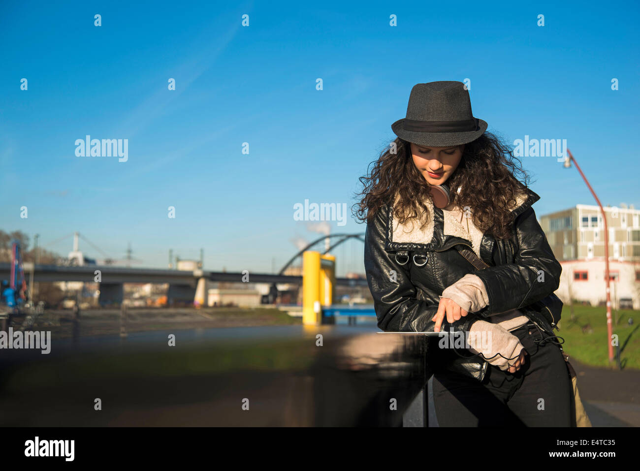 Teenage girl standing outdoors, wearing fedora and using tablet ...