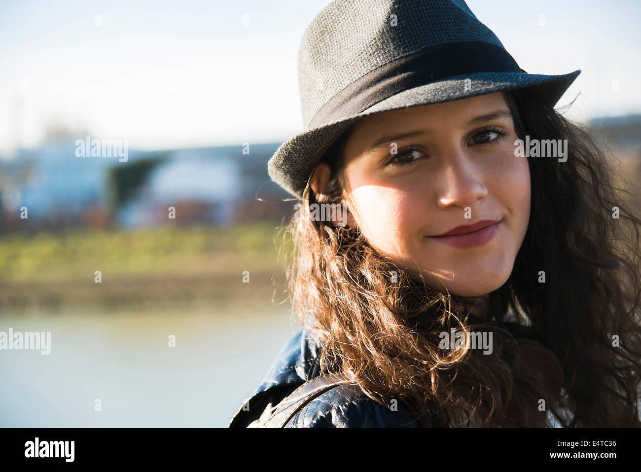 Close-up portrait of teenage girl outdoors, wearing fedora, smiling and ...