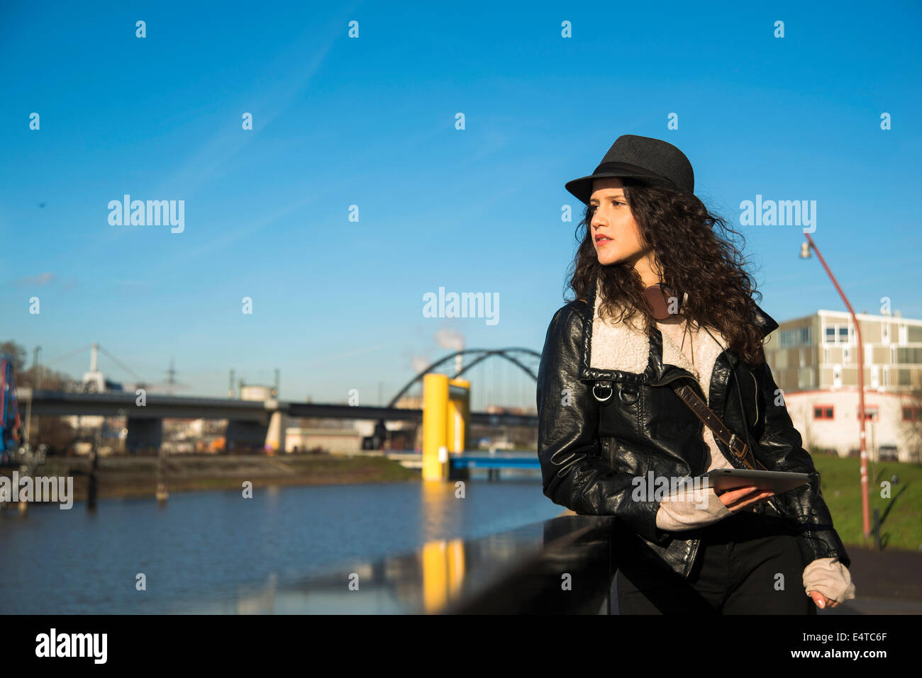 Teenage girl standing outdoors, wearing fedora and holding tablet ...