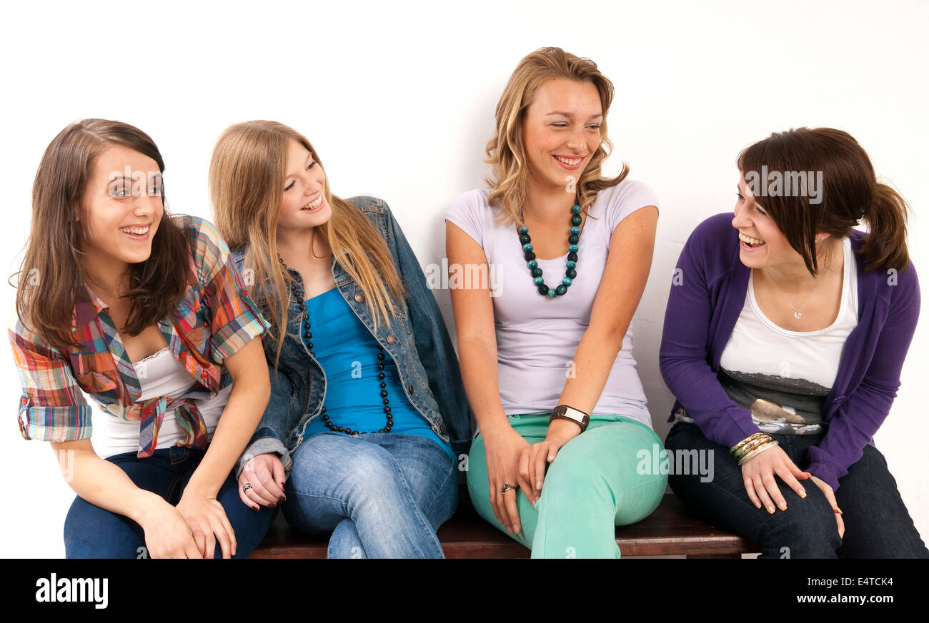 Four, young women sitting on bench together, laughing and looking at ...