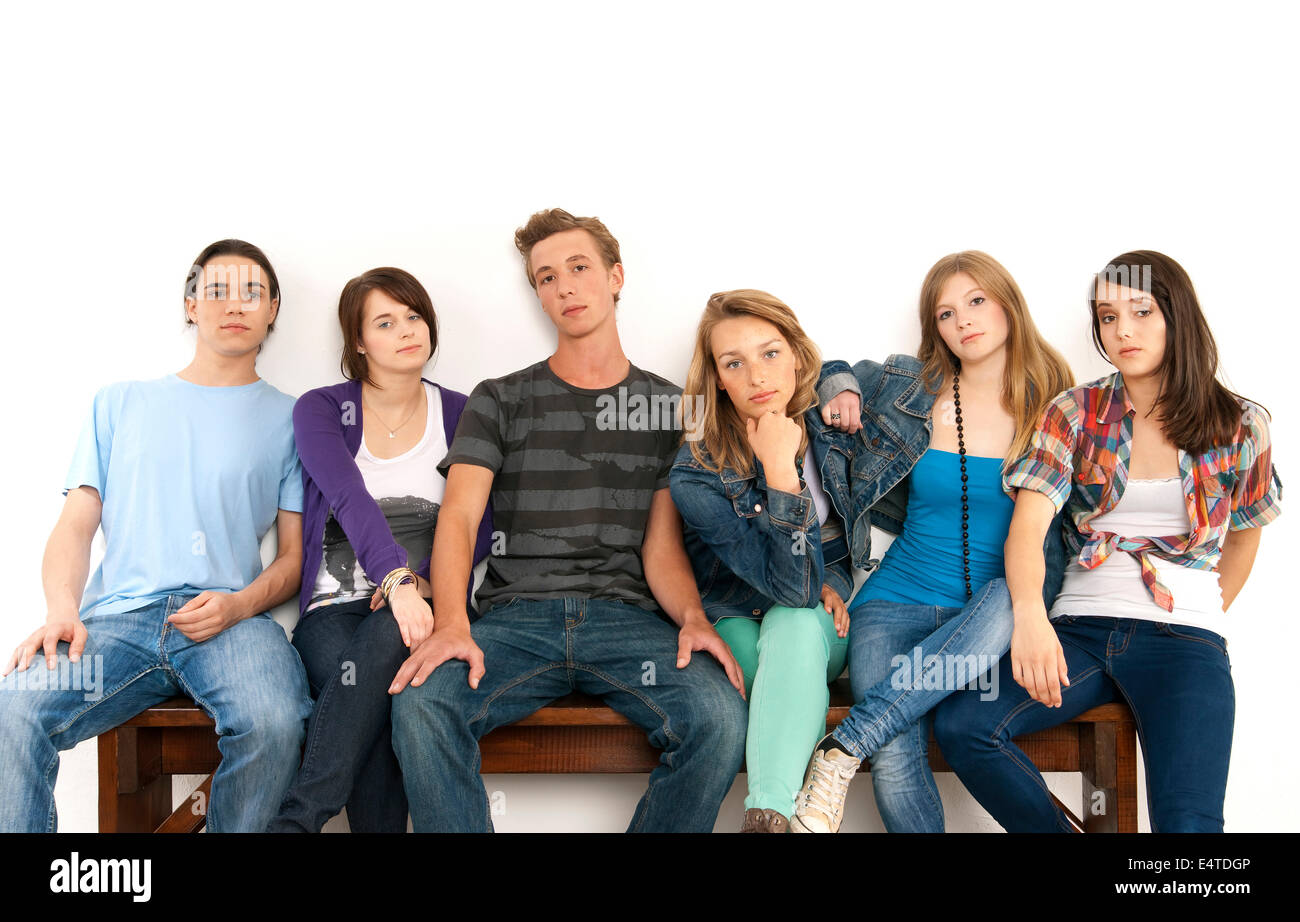 Portrait of six young people sitting together on a bench, studio shot ...