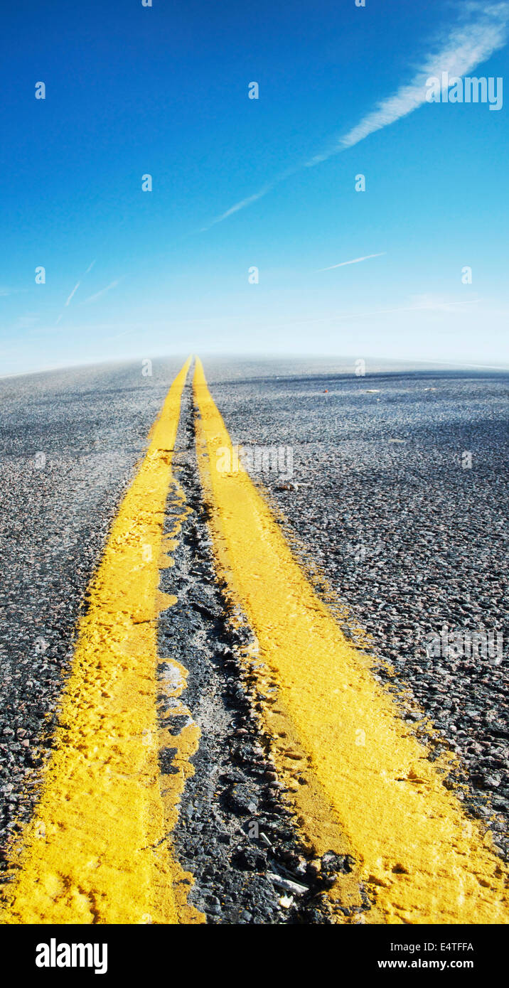 Close-up view of yellow center lines on deserted highway with blue sky ...