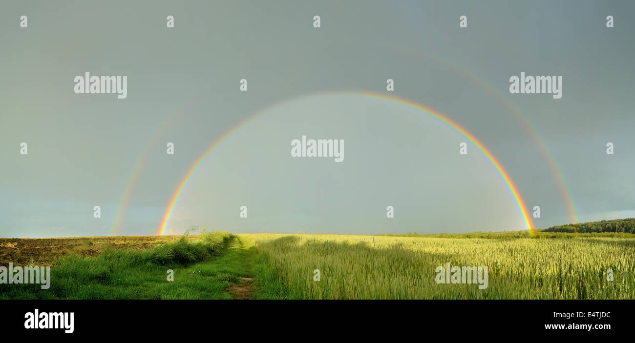 Double full rainbow over country road. Rainbow over blue sky and green ...