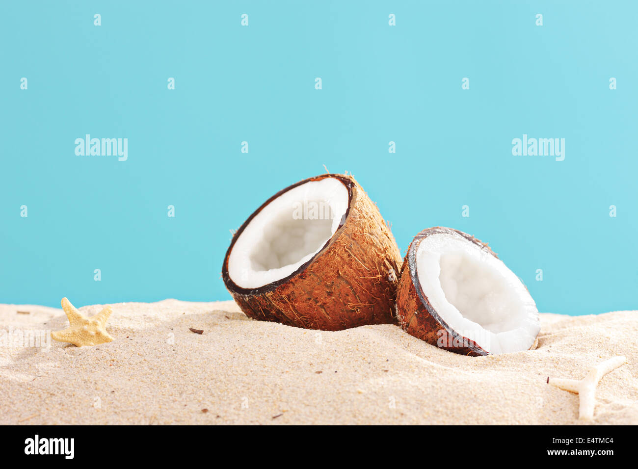 Studio shot of a sliced coconut on a sandy surface on blue background ...
