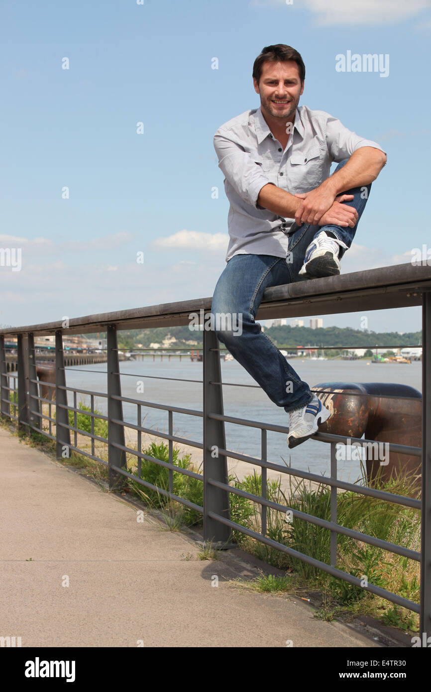 Man sitting on riverside railing Stock Photo - Alamy