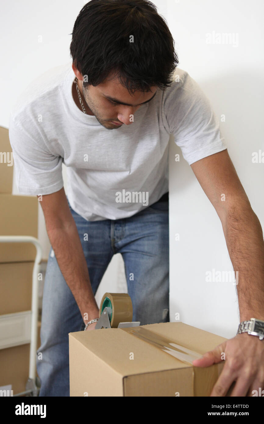 Young man taping shut a cardboard box Stock Photo - Alamy