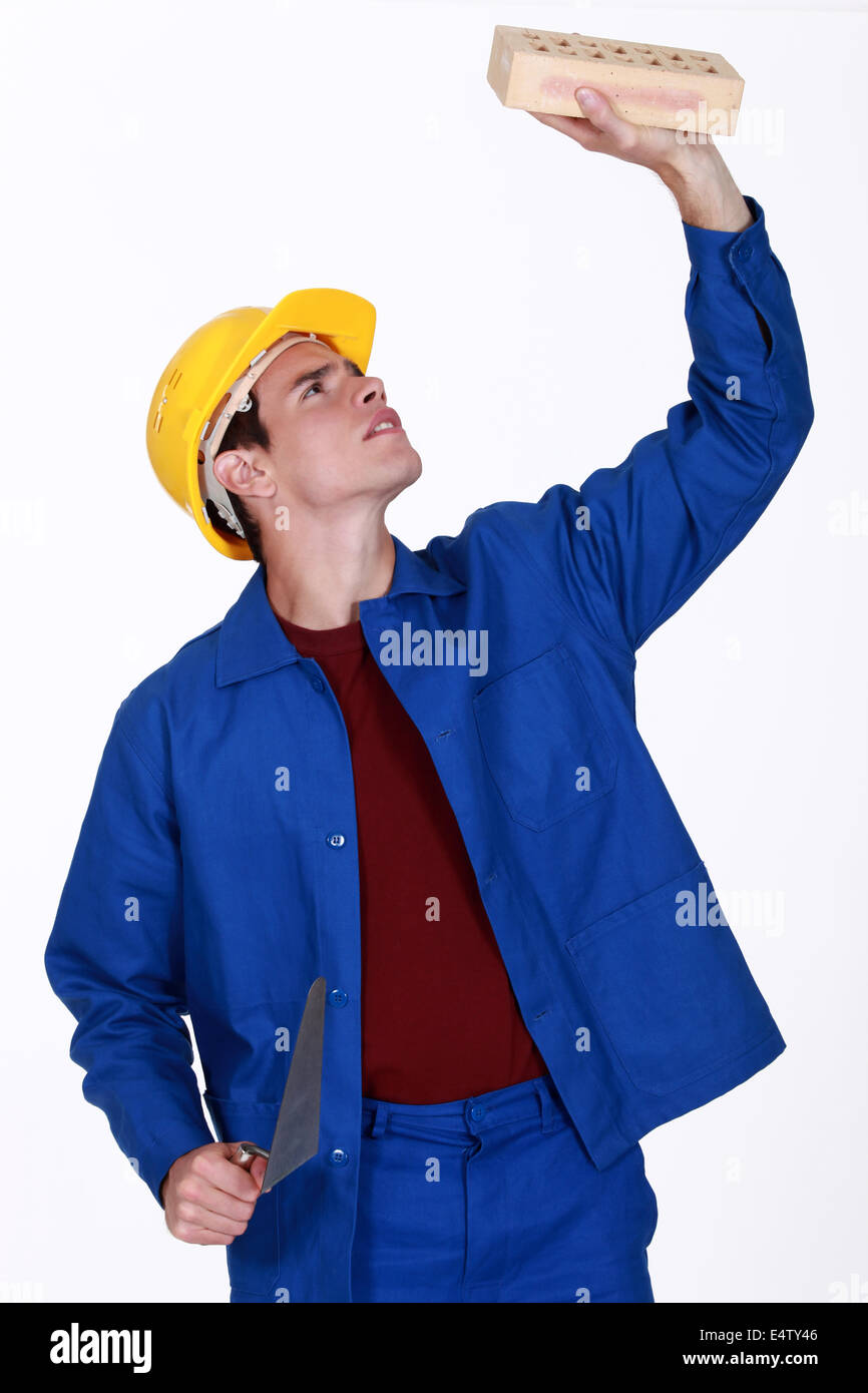 young bricklayer in jumpsuit inspecting brick Stock Photo - Alamy