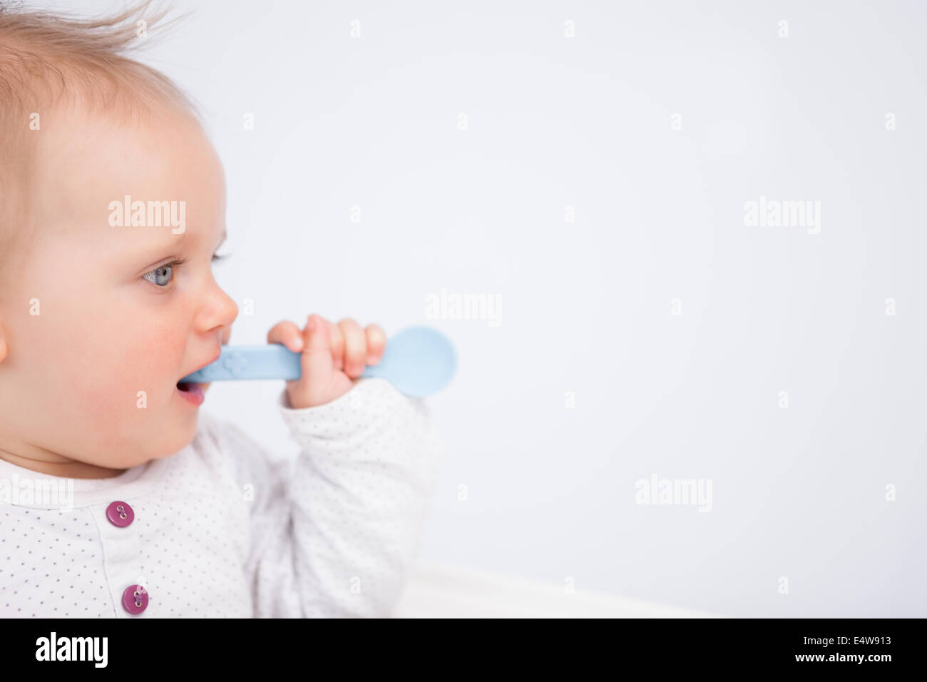Cute baby biting a blue spoon Stock Photo - Alamy