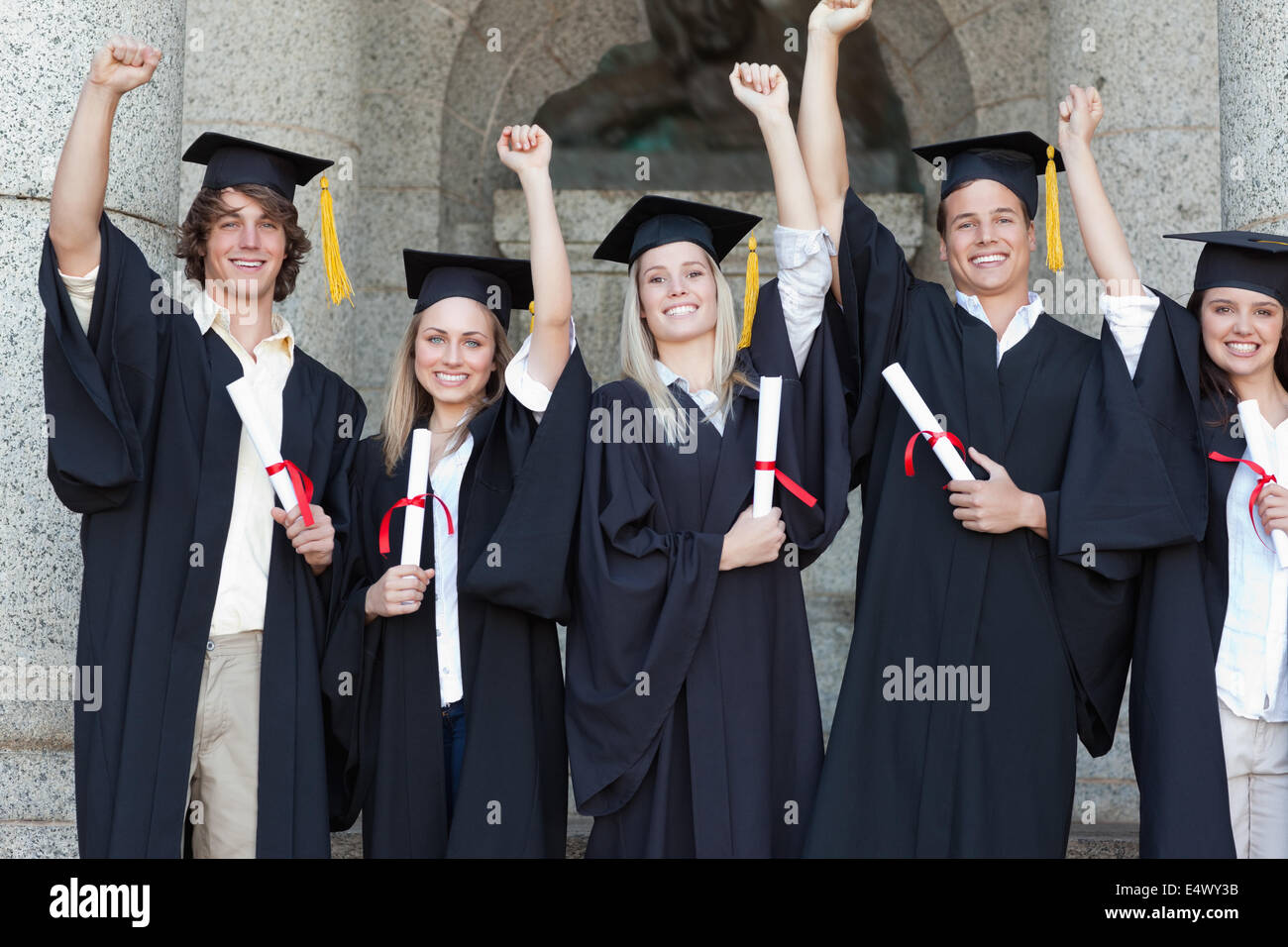 Smiling graduates posing while raising arms Stock Photo - Alamy