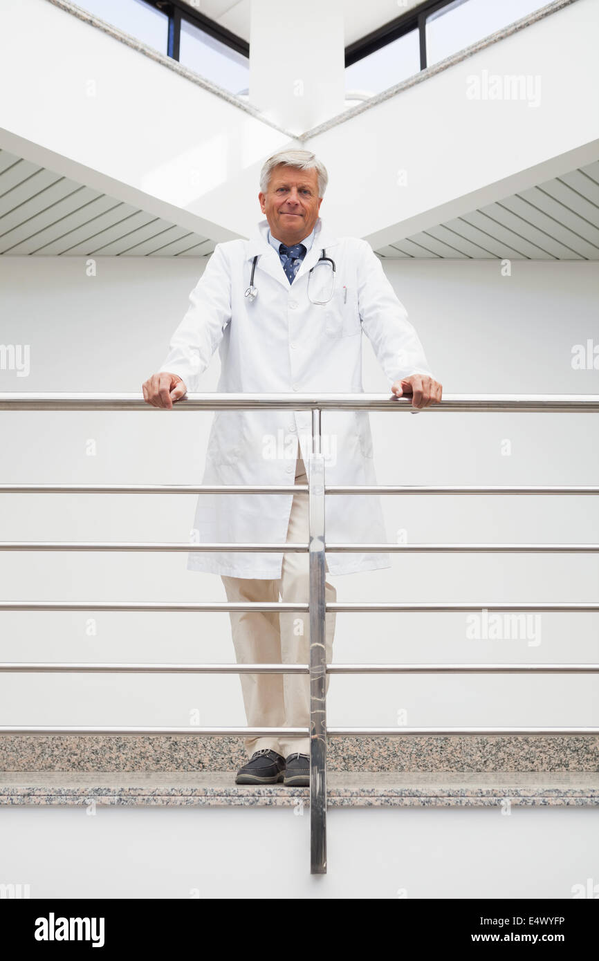 Smiling doctor leaning against rail Stock Photo - Alamy