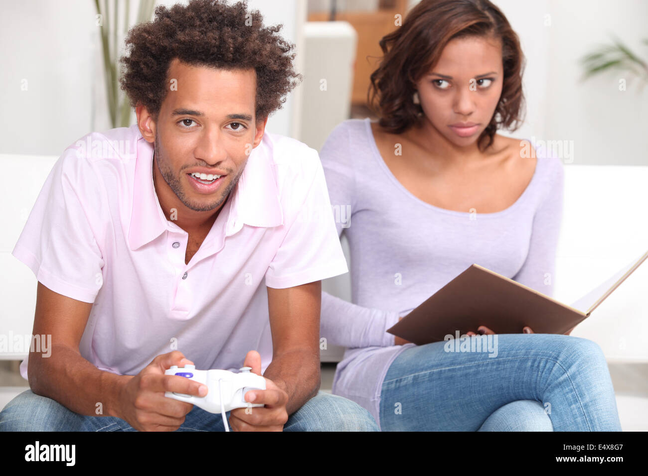 Man playing video games and woman reading Stock Photo - Alamy